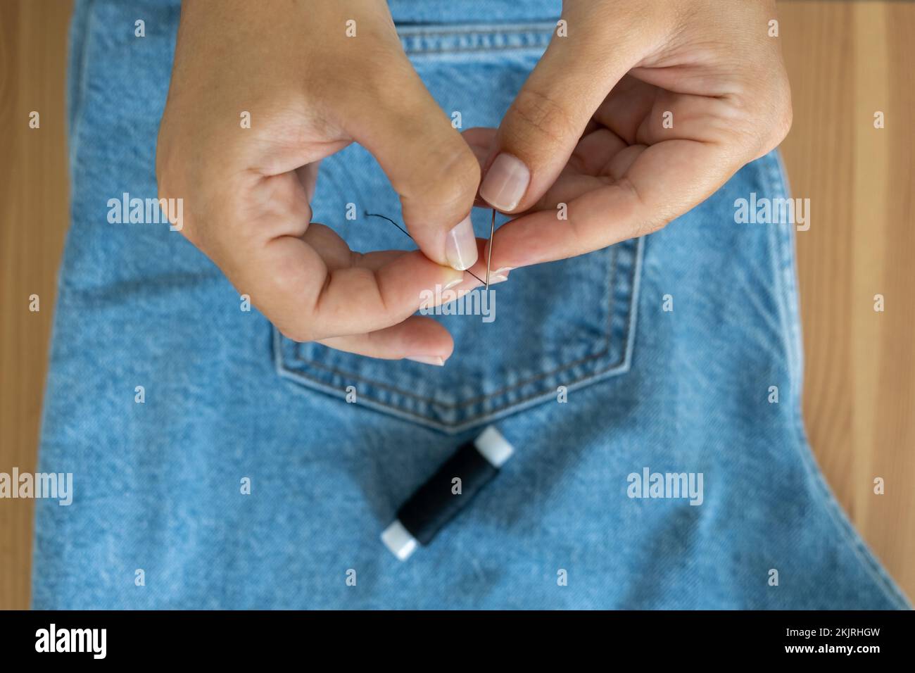 Hands of a seamstress threading a needle on the background of jeans ...