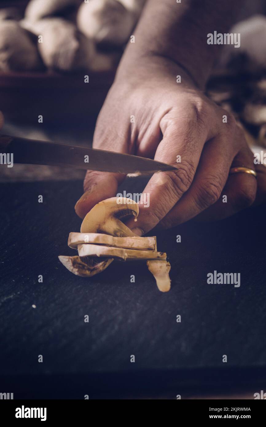 A vertical shot of a cook cutting raw fresh button mushrooms on the ...