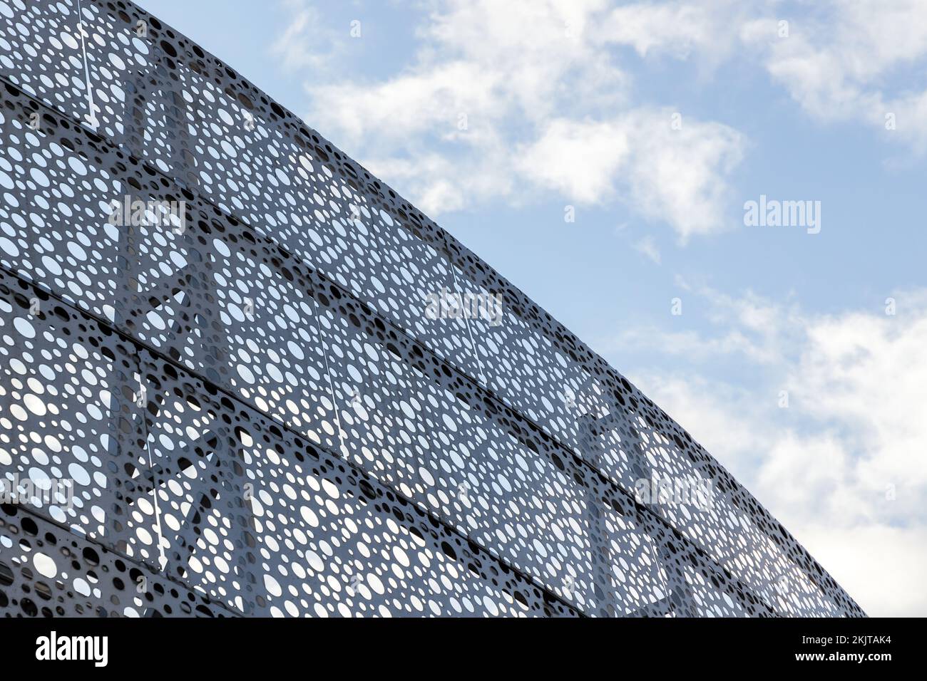 Decorative metal wall with round holes pattern under cloudy blue sky ...