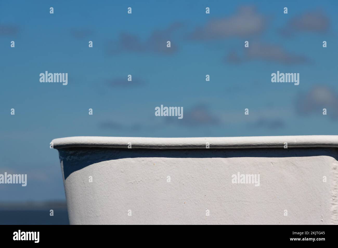 Close up side view of bow of a white ship hull against blue sky with ...