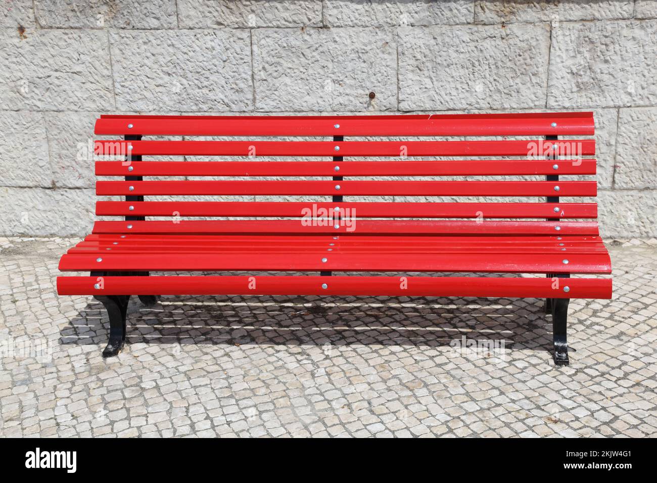 A bright red park bench with stone wall background Stock Photo - Alamy