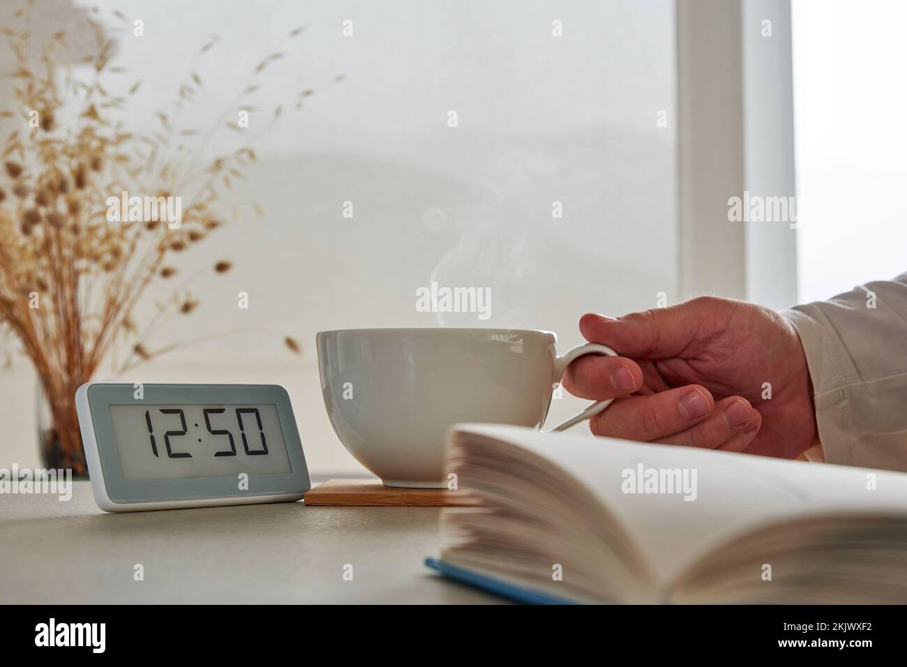 Man reading book and drinking hot coffee on the table in the kitchen ...