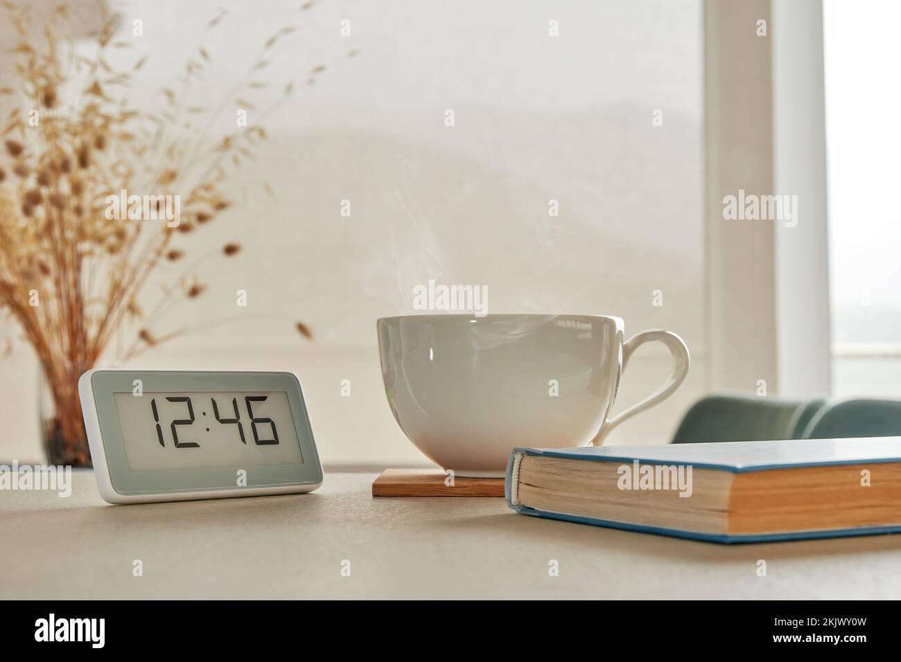 Cozy home desk with hot coffee mug, book and clocks. Wide window with ...