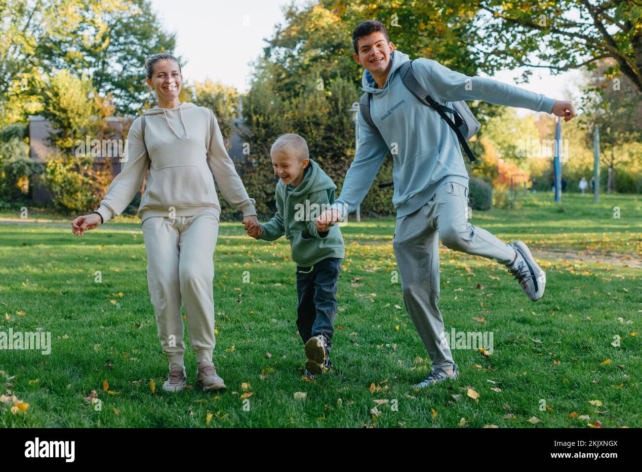 a family mom and 2 sons are having fun, running in the park and jumping ...