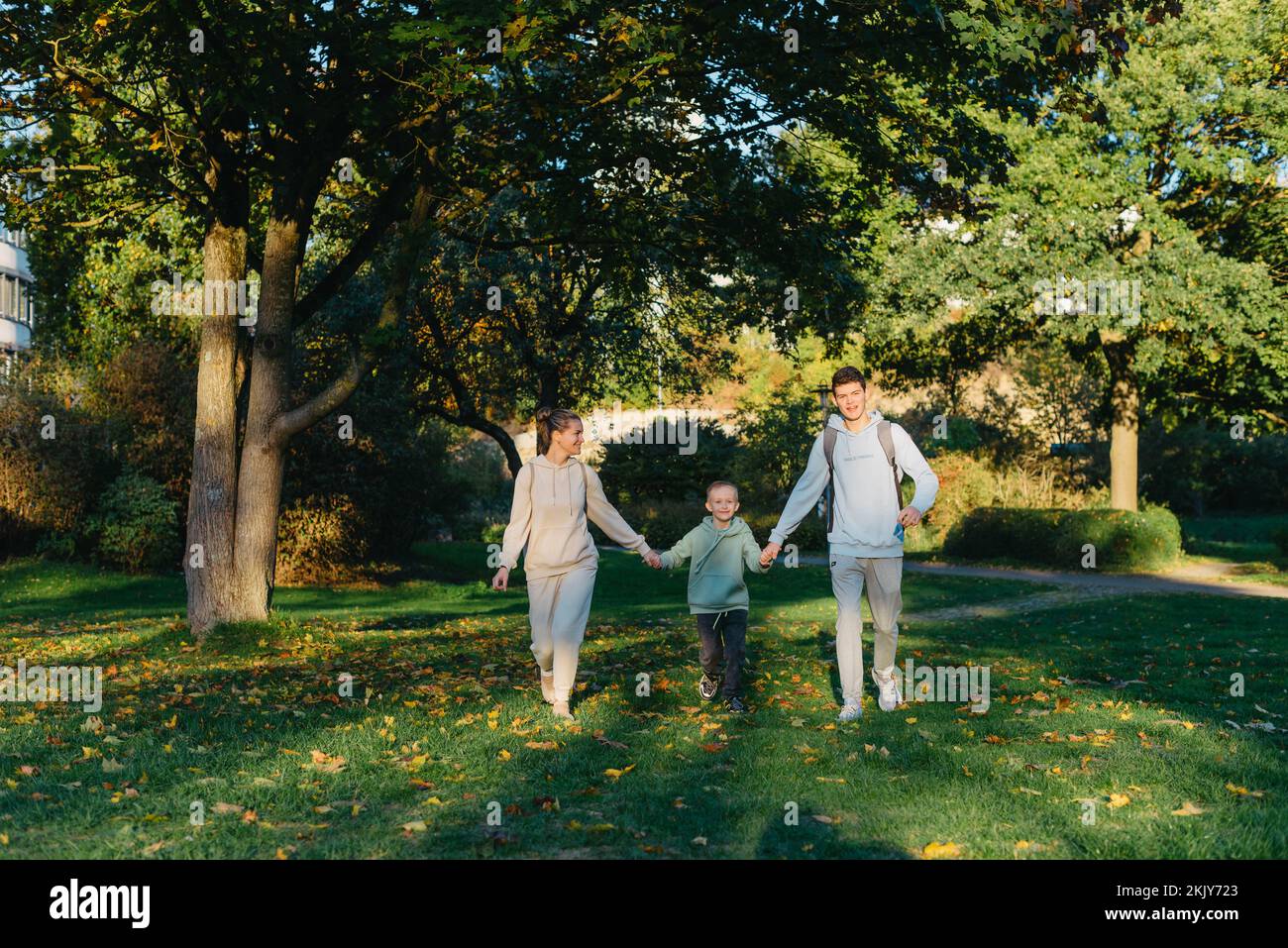 a family mom and 2 sons are having fun, running in the park and jumping ...