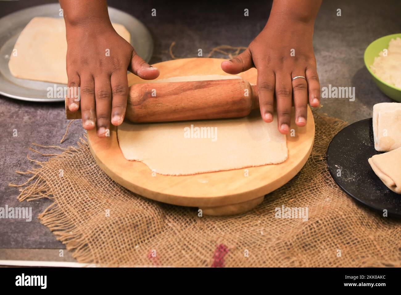 A closeup shot of a woman stretching a dough with a rolling pin on a ...