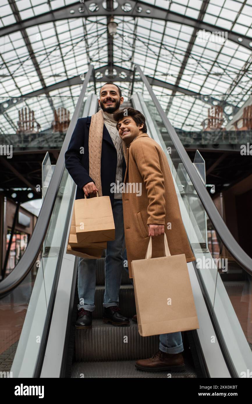 low angle view of cheerful gay men in stylish casual clothes holding ...