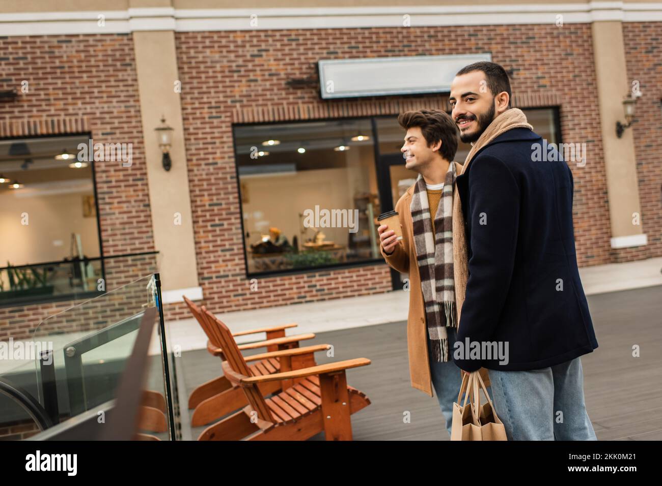 stylish gay men with shopping bags and coffee to go standing near ...