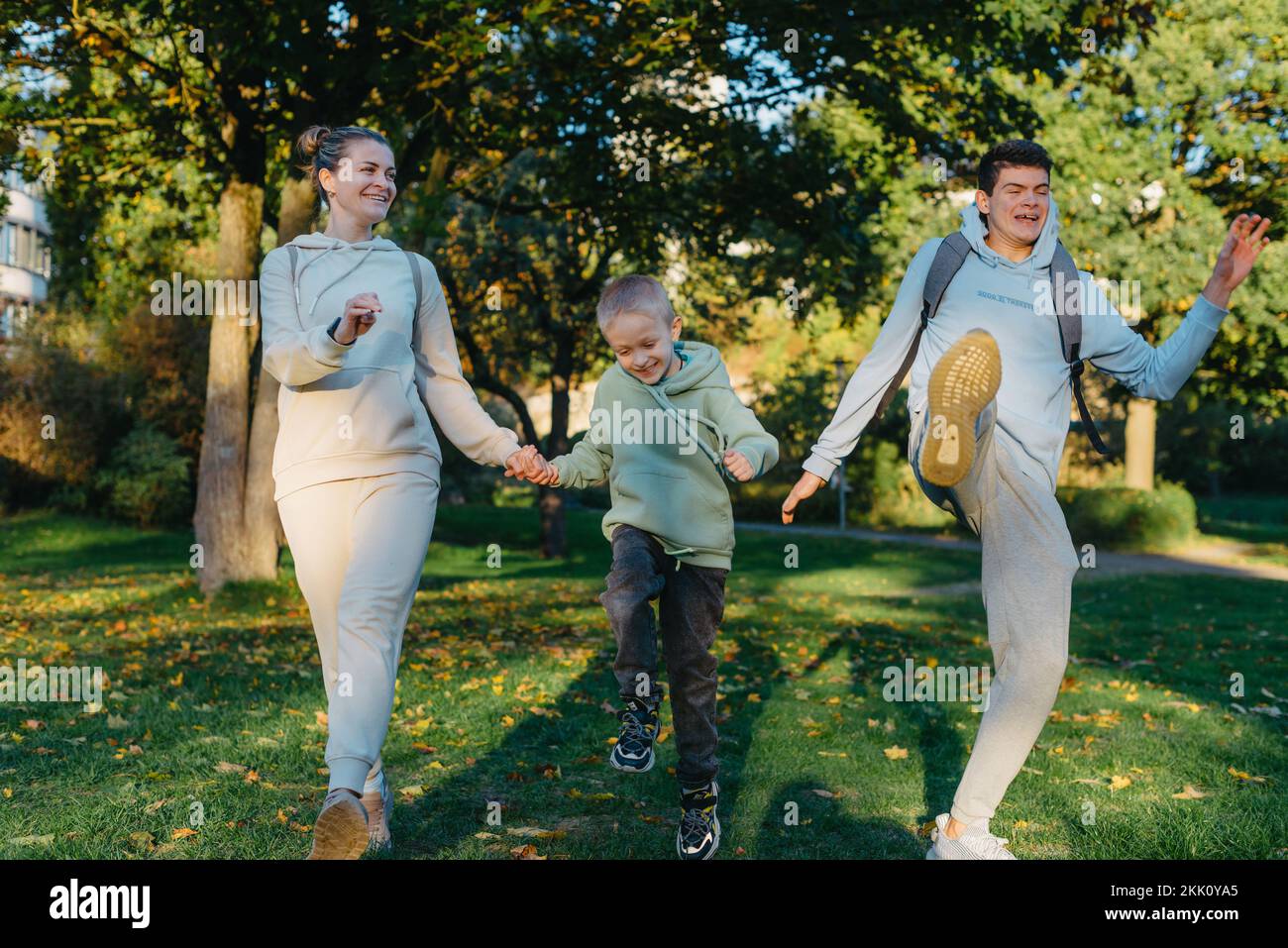 a family mom and 2 sons are having fun, running in the park and jumping ...