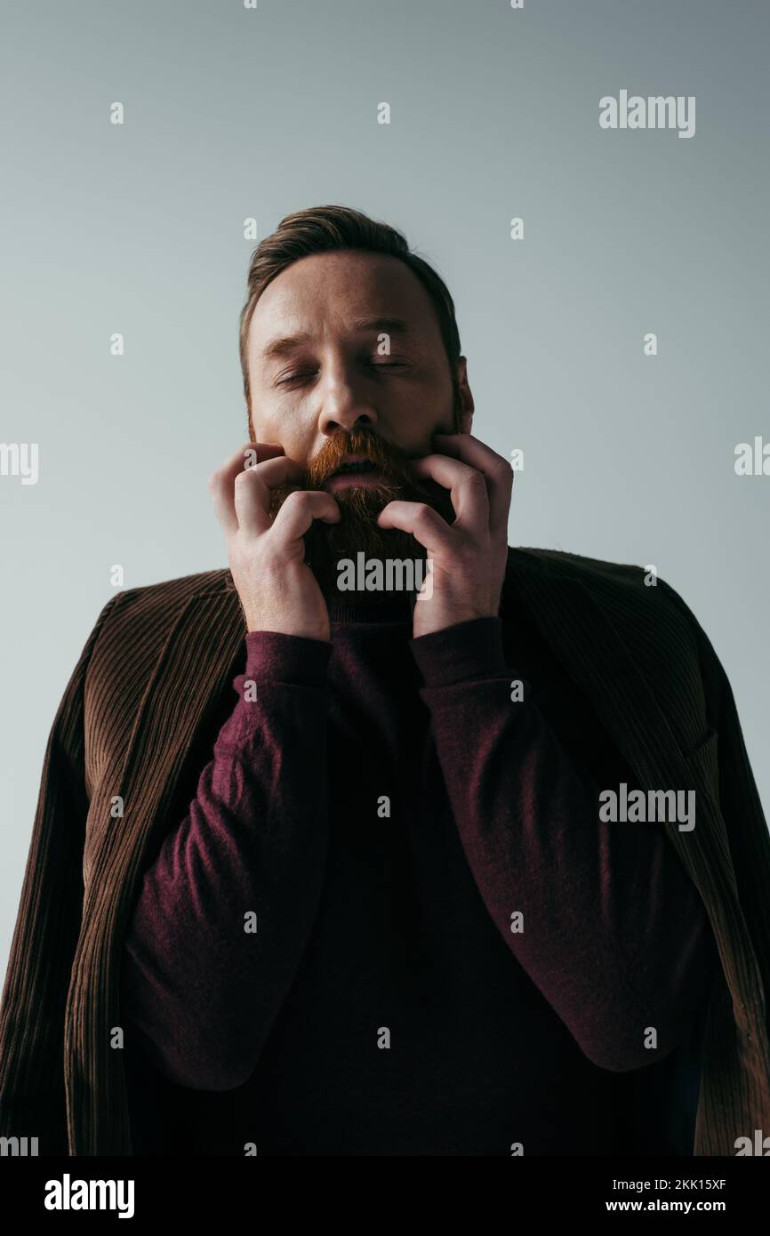 man in turtleneck and blazer scratching beard isolated on grey,stock ...