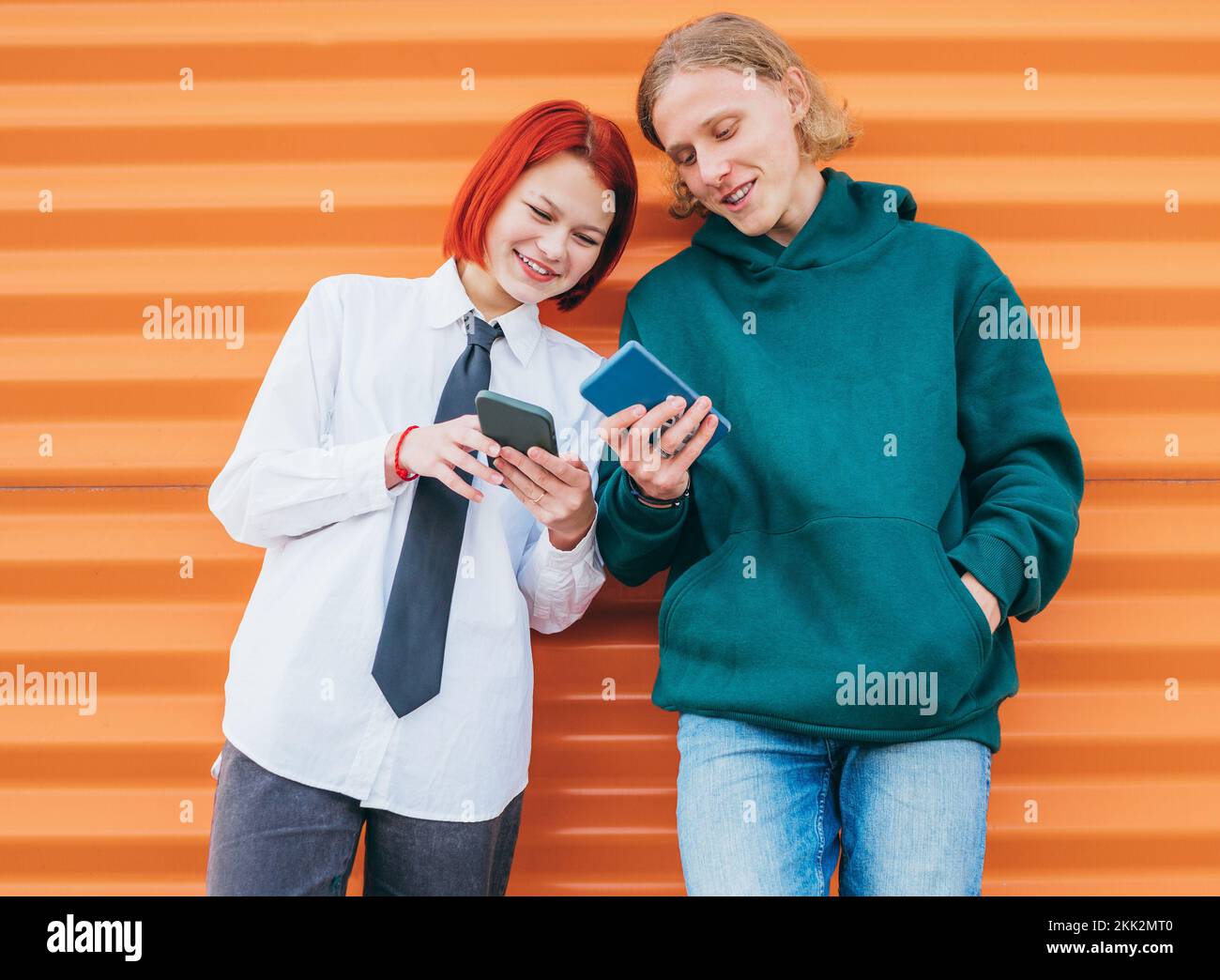 Two caucasian teen friends boy and a girl browsing their smartphone ...
