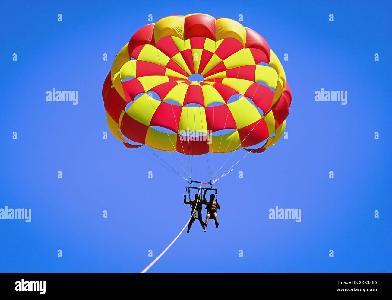 A low-angle shot of two people riding a parasail under a clear blue sky ...