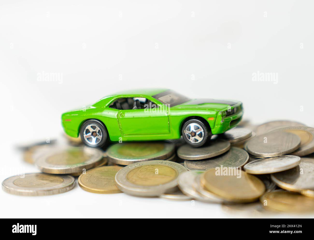 Green toy car is on a pile of money coins pile , isolated on white ...