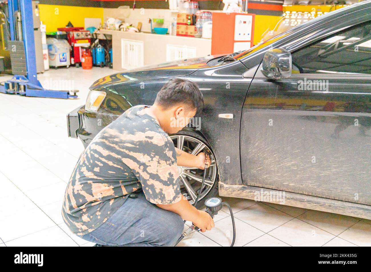 Technician filling the air on car wheel after repair tire in garage ...