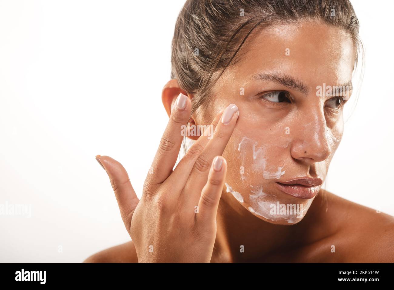 Beautiful brunette model smearing cream on her face at the studio on a ...