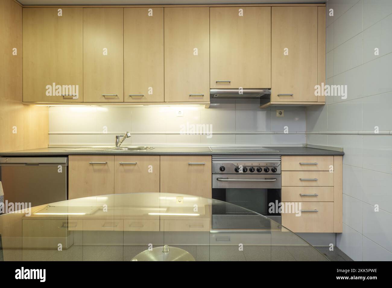 Wall of a kitchen lined with beech wood cabinets, a gray countertop and ...