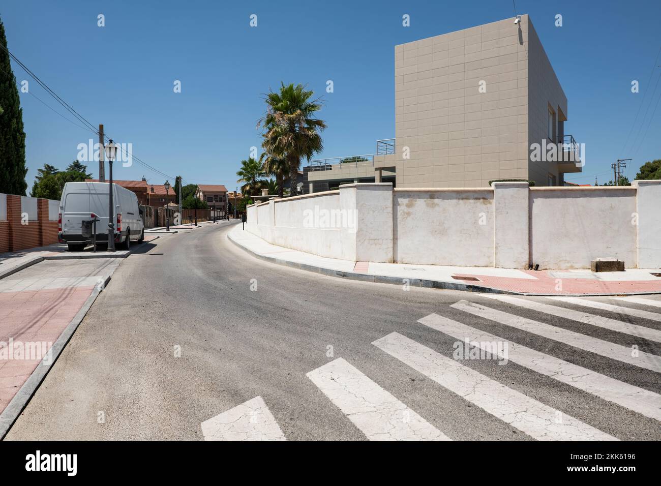 A street in an urbanization with a curved zebra crossing and palm trees ...