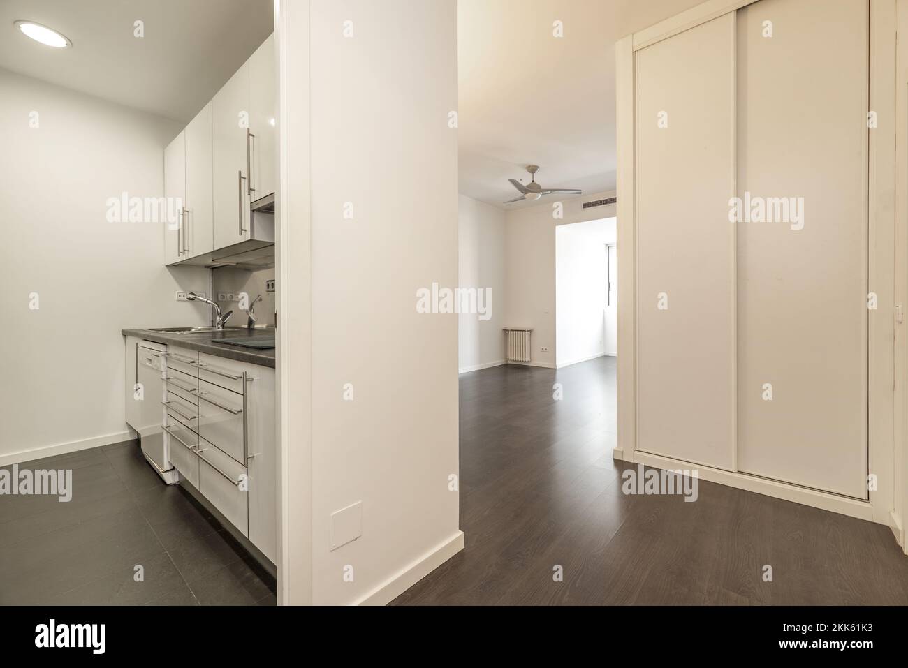 Small kitchen of a studio apartment with dark floors and white built-in ...