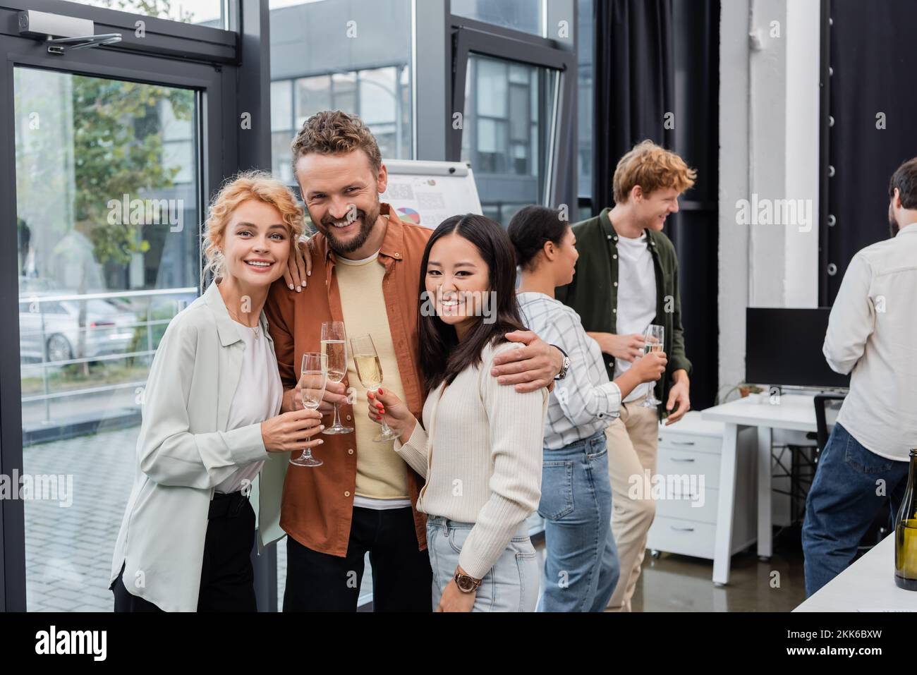 Positive businessman hugging multiethnic colleagues with champagne in ...