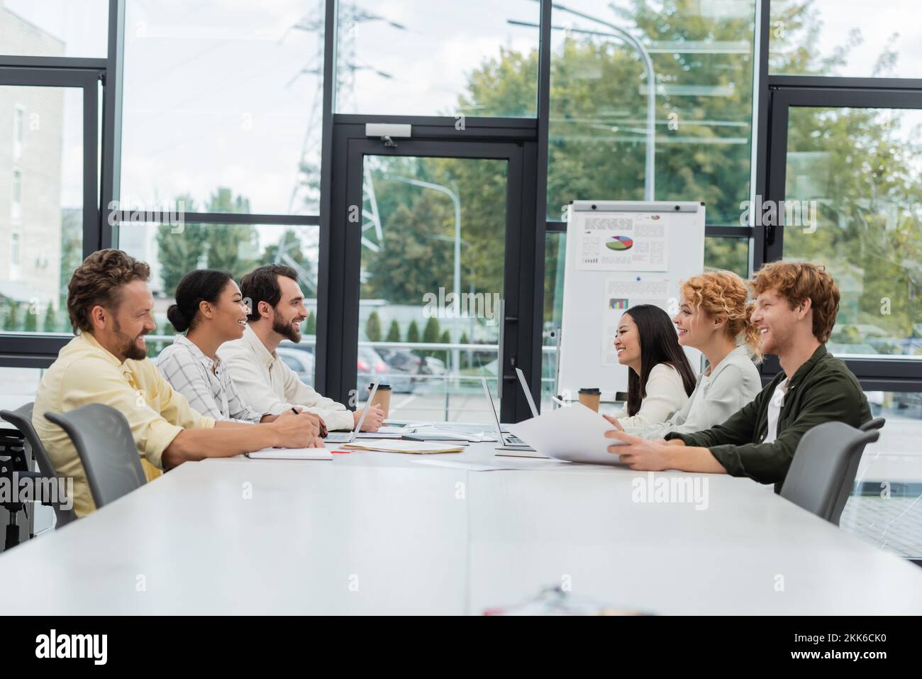 multiethnic corporate team sitting at conference table near flip chart ...
