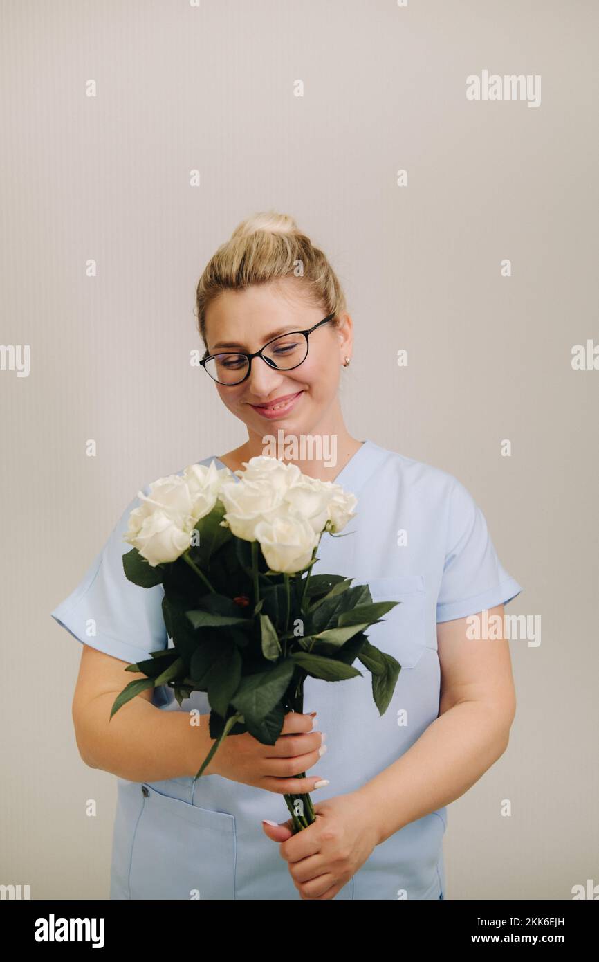 A female doctor in a blue robe with a bouquet of white roses in her ...