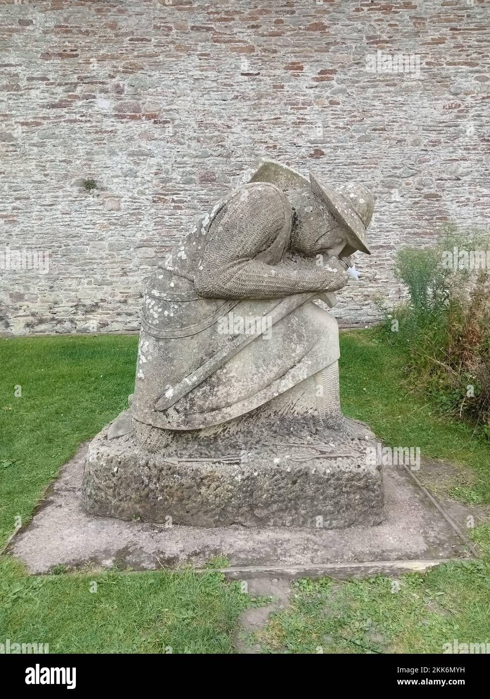 The vertical shot of an aged statue of a warrior before the old wall ...