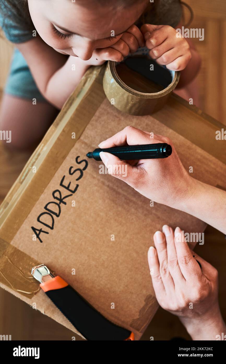 Woman writing an address on a cardboard box parcel in room at home ...