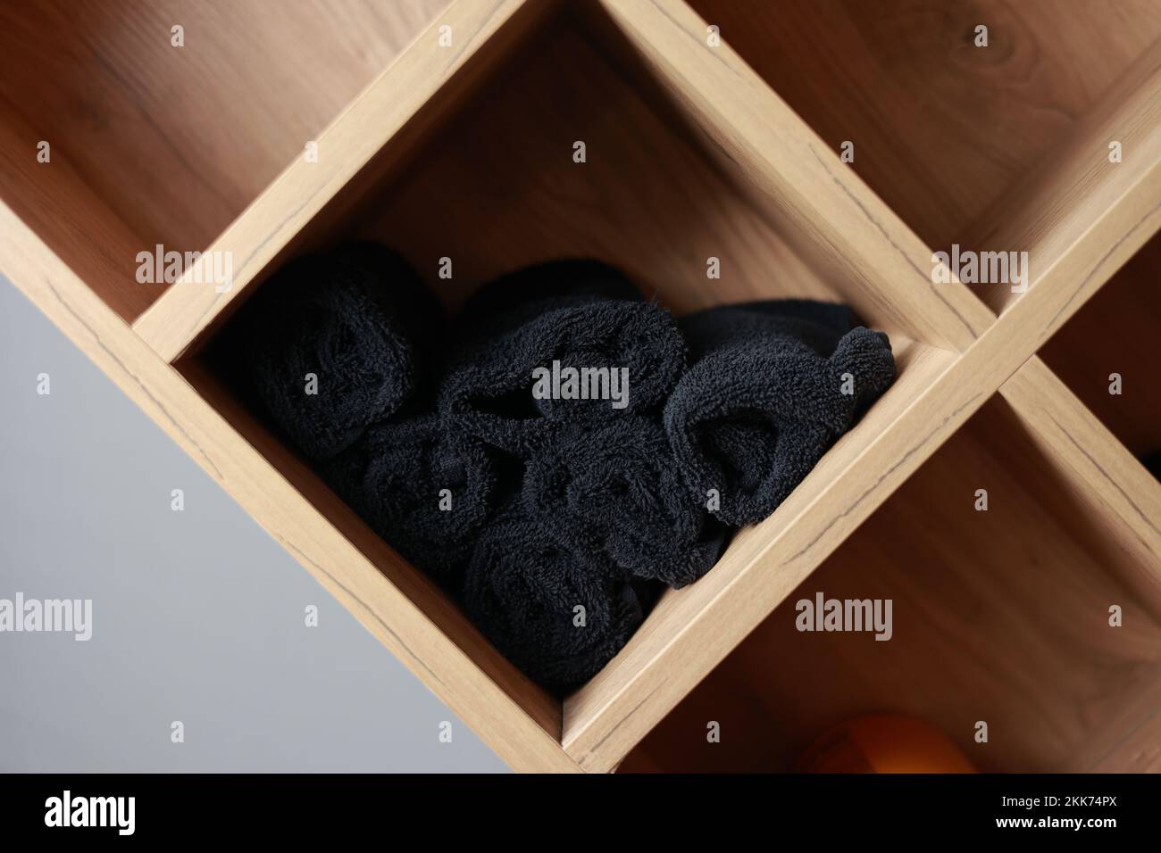 Stack of many clean black towels on two wooden shelves on white wall ...