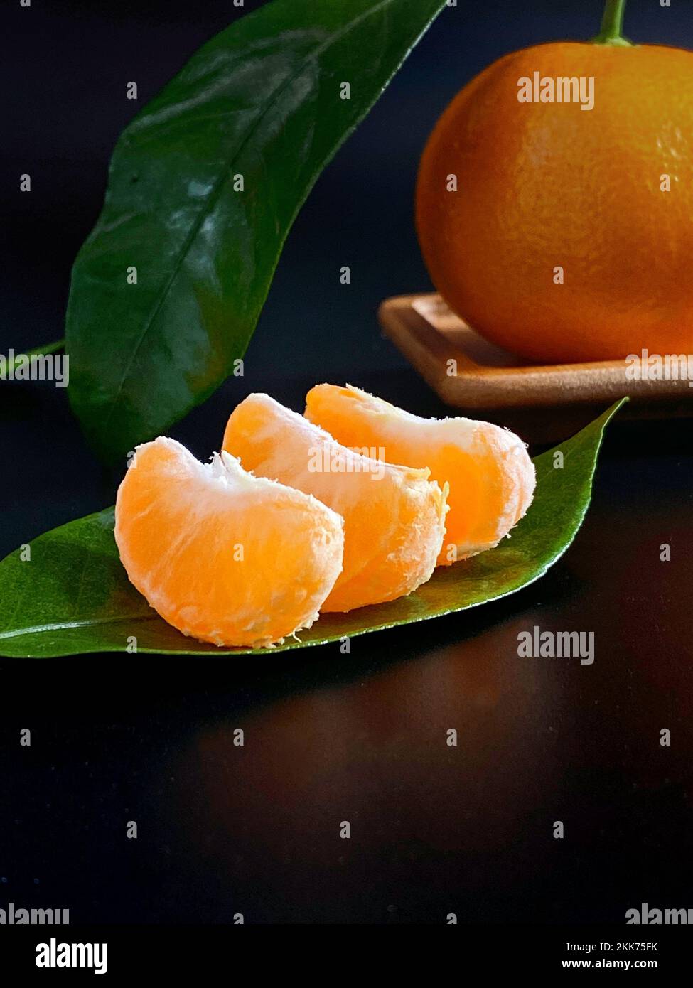 Vertical closeup of peeled tangerine on green leaf and whole tangerine ...