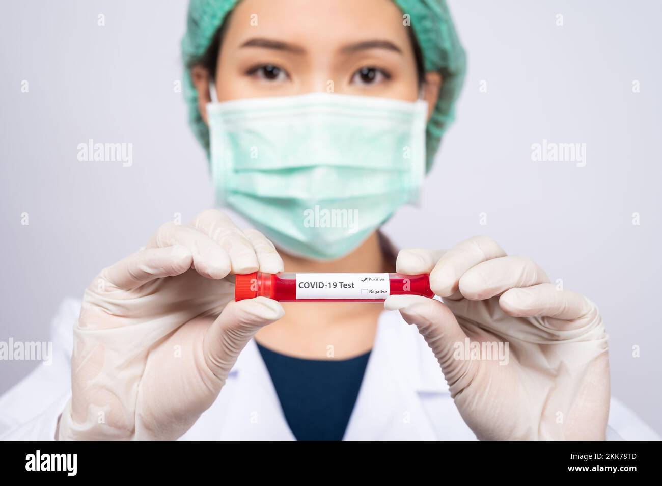 A young Asian doctor holding blood sample test tube on white background ...