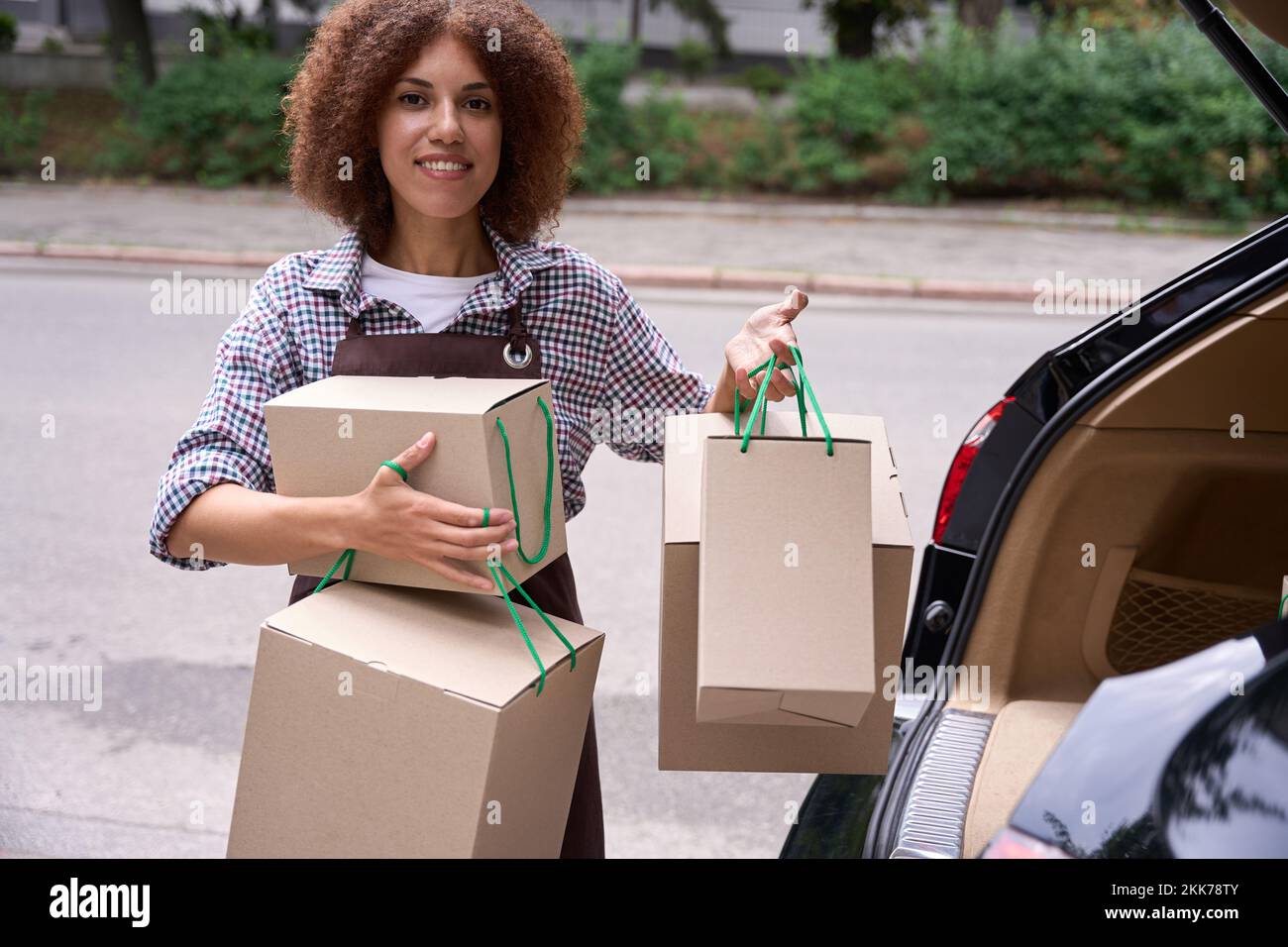 Cheerful young woman unloading car with delivery for business Stock ...