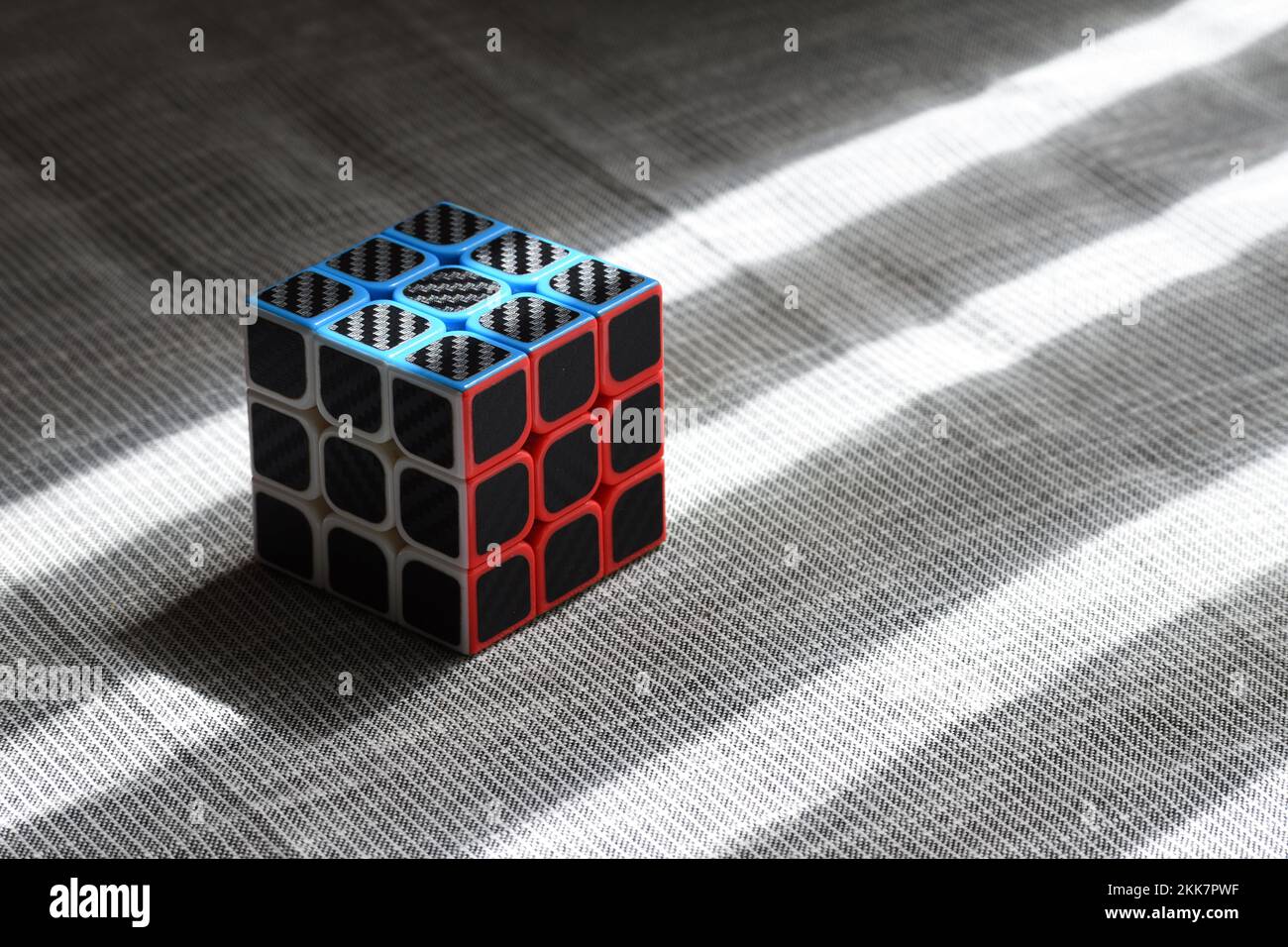 A closeup of a black Rubik's cube with red and blue lines on the sunlit ...