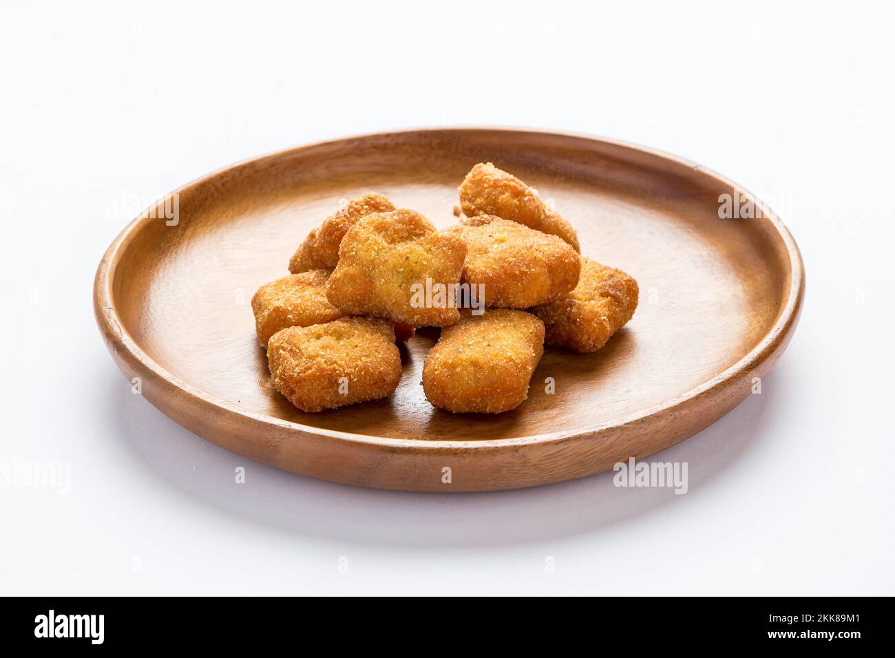 An isolated shot of crispy nuggets on a wooden plate on a white ...