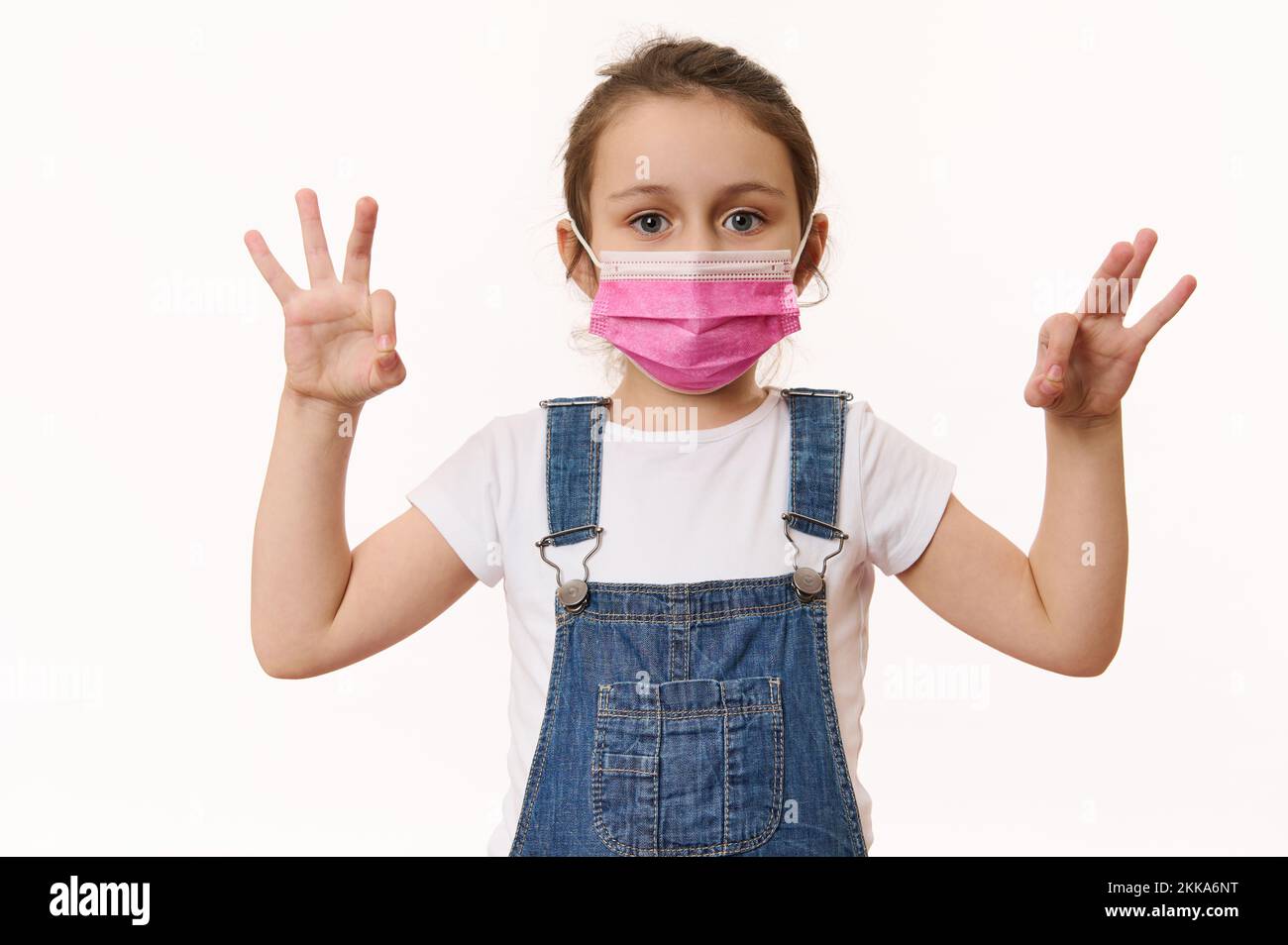 Little girl wearing pink protective medical mask, gestures with hands ...