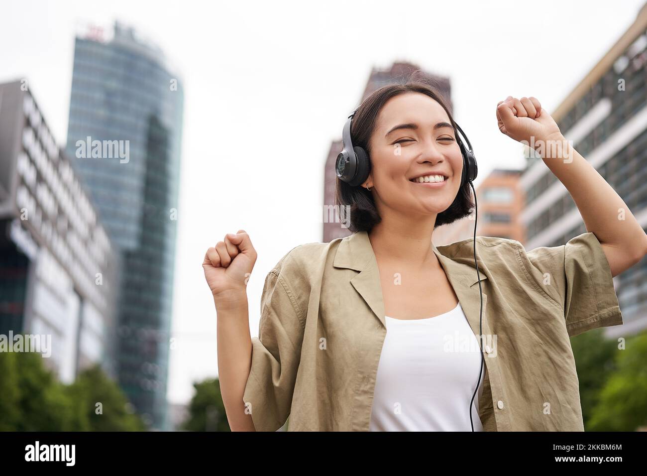 Happy asian woman in headphones, listening music and dancing on street ...