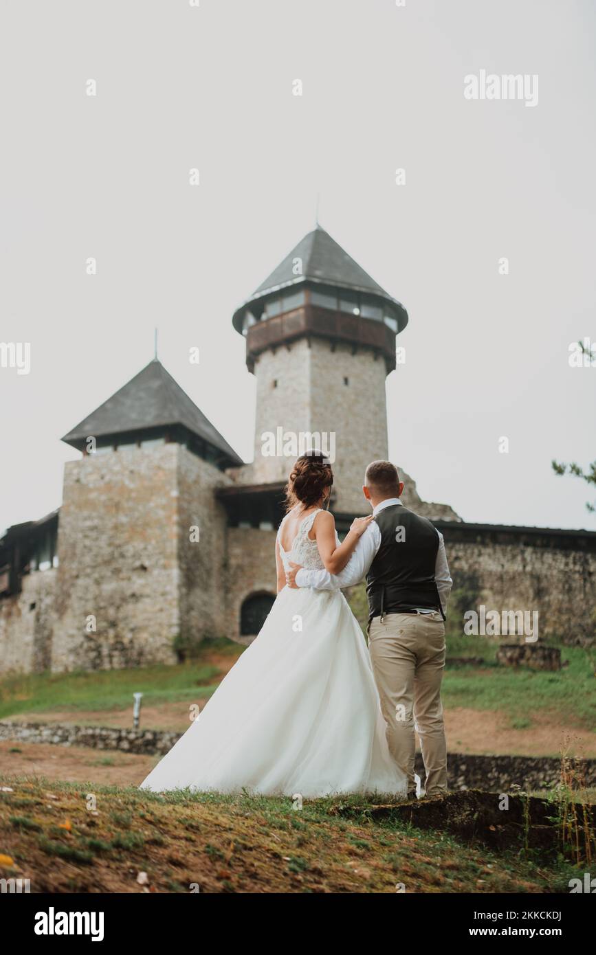 A vertical shot of a bride and a groom standing against an old church ...