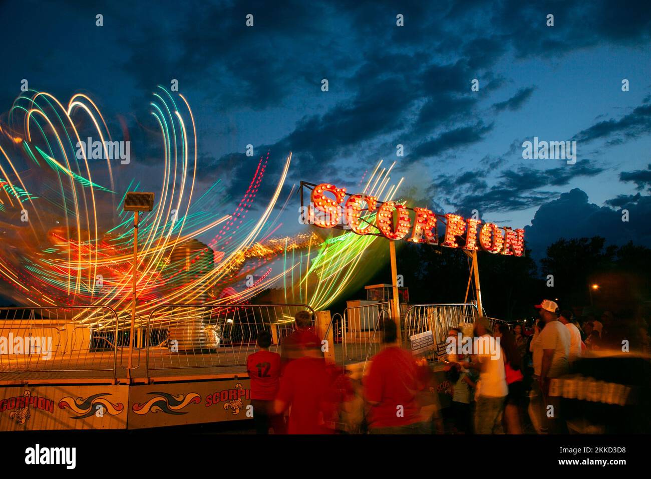 A long exposure of people looking at a carnival ride lighting up the ...
