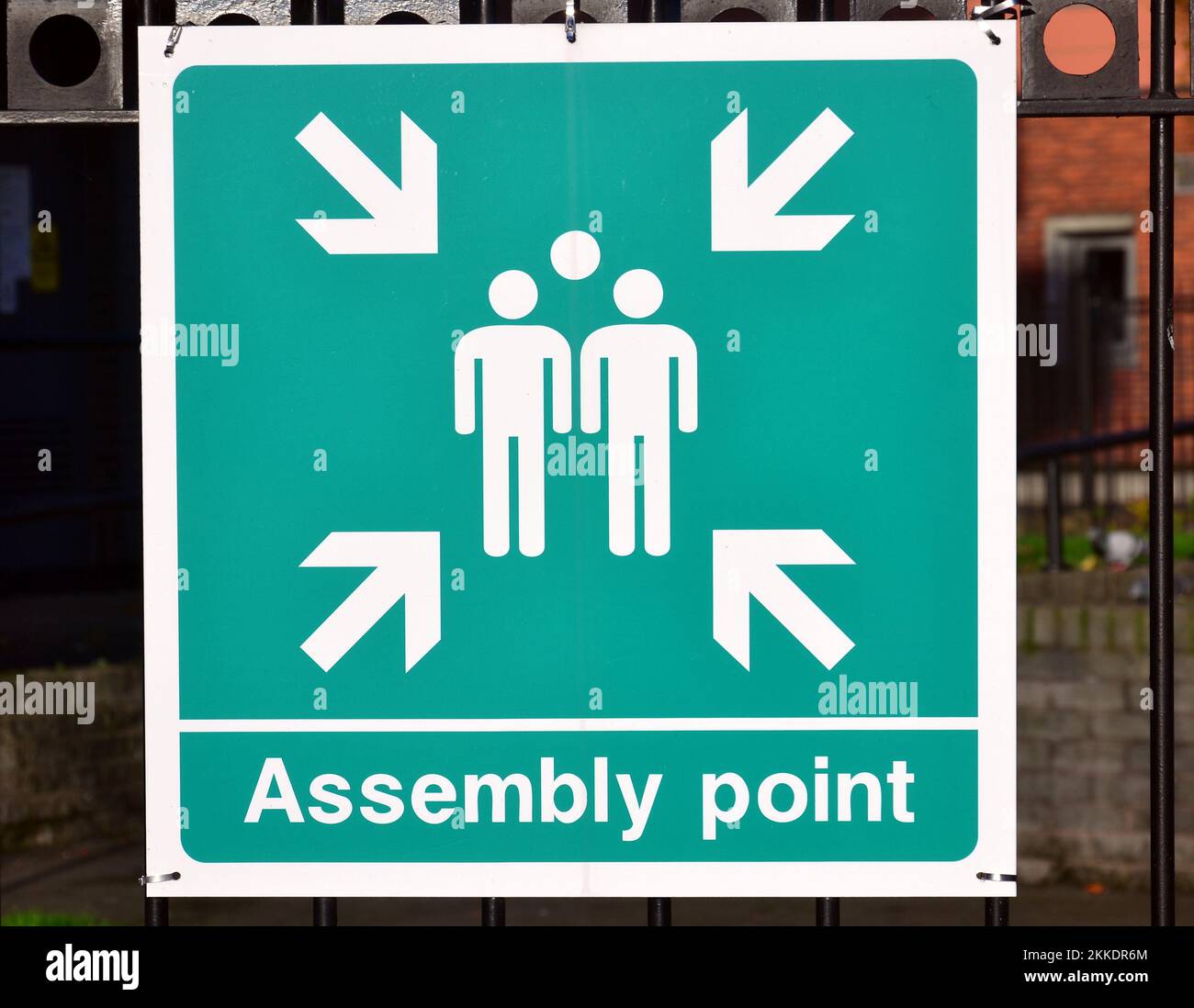 An 'assembly point' sign contains two people images and arrows pointing ...