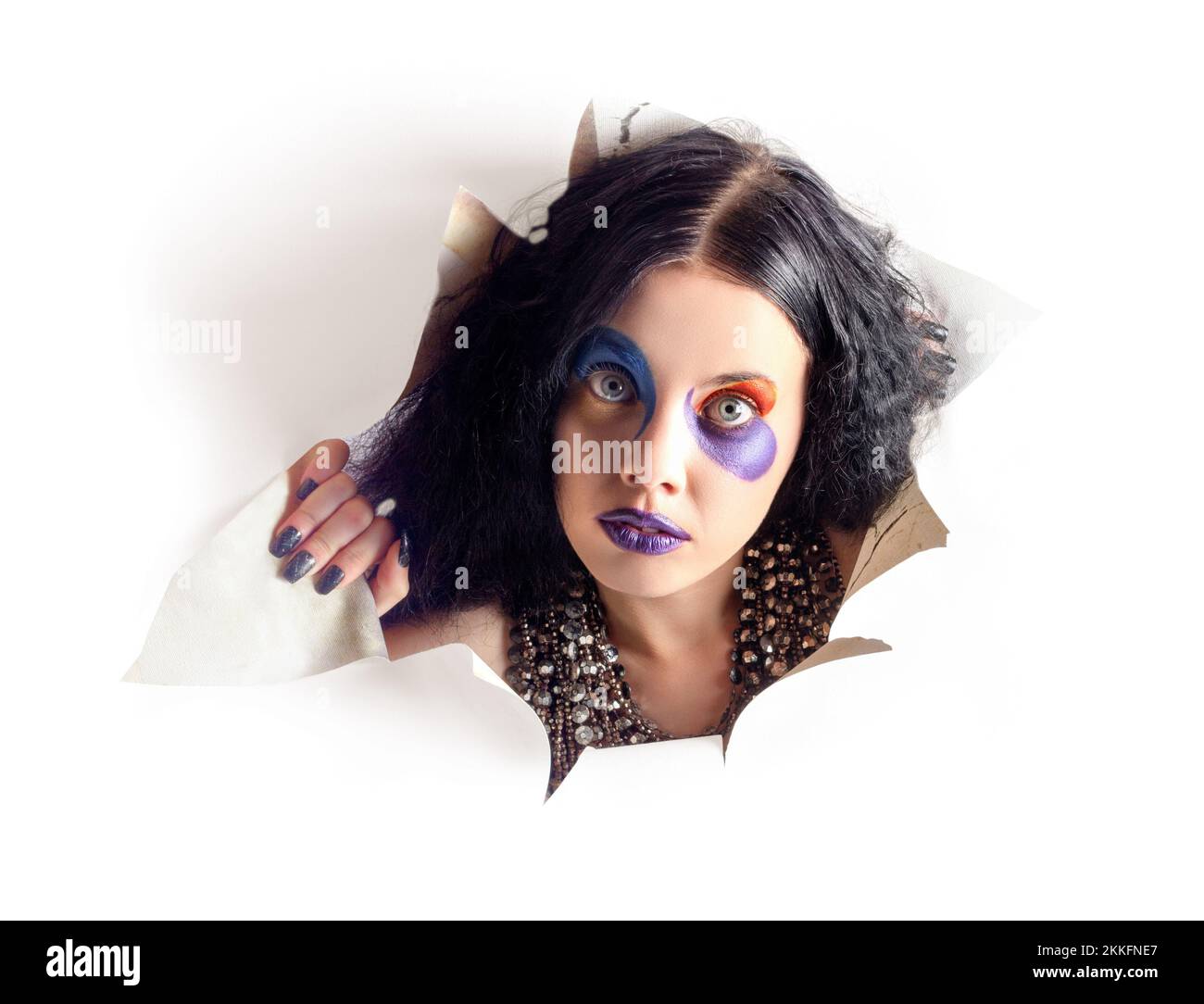 Young woman with colorful face makeup looking through ripped hole on ...