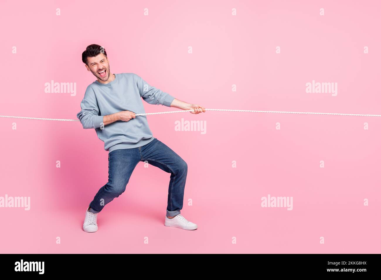 Full length photo of excited guy playing tug war game pull string ...