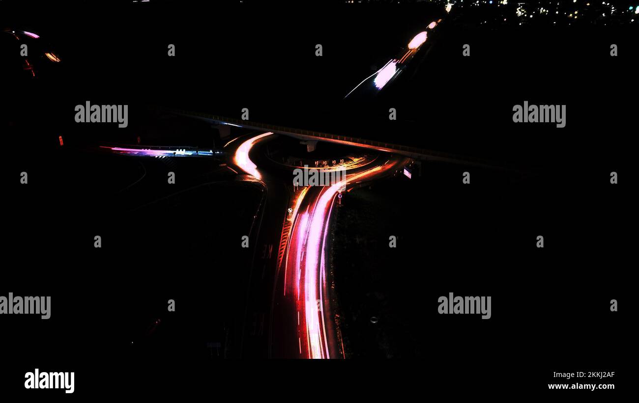 An aerial view of a roundabout road at night with long exposure red car ...