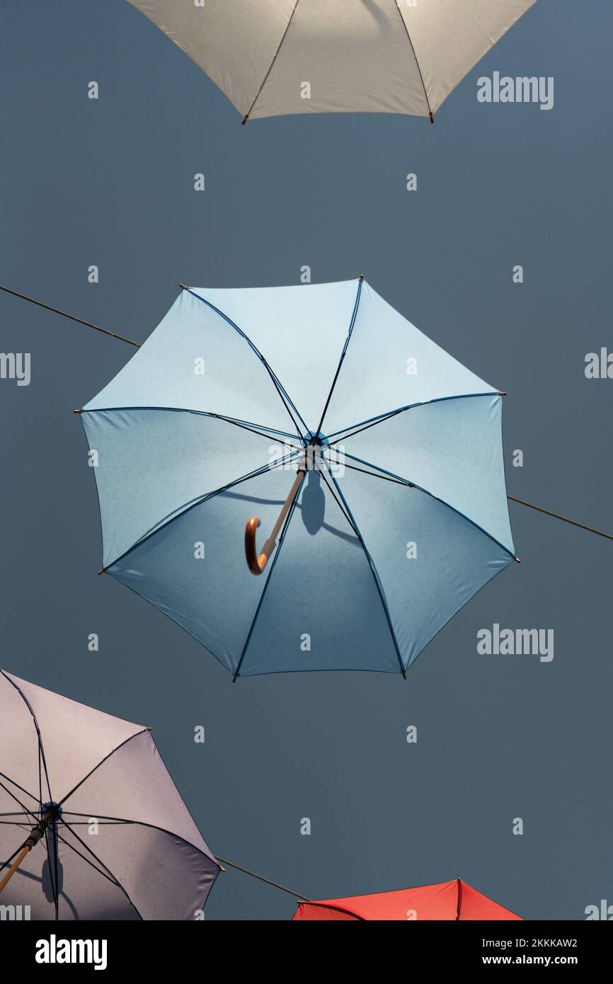 Colorful umbrellas fixed on steel ropes between buildings against blue ...