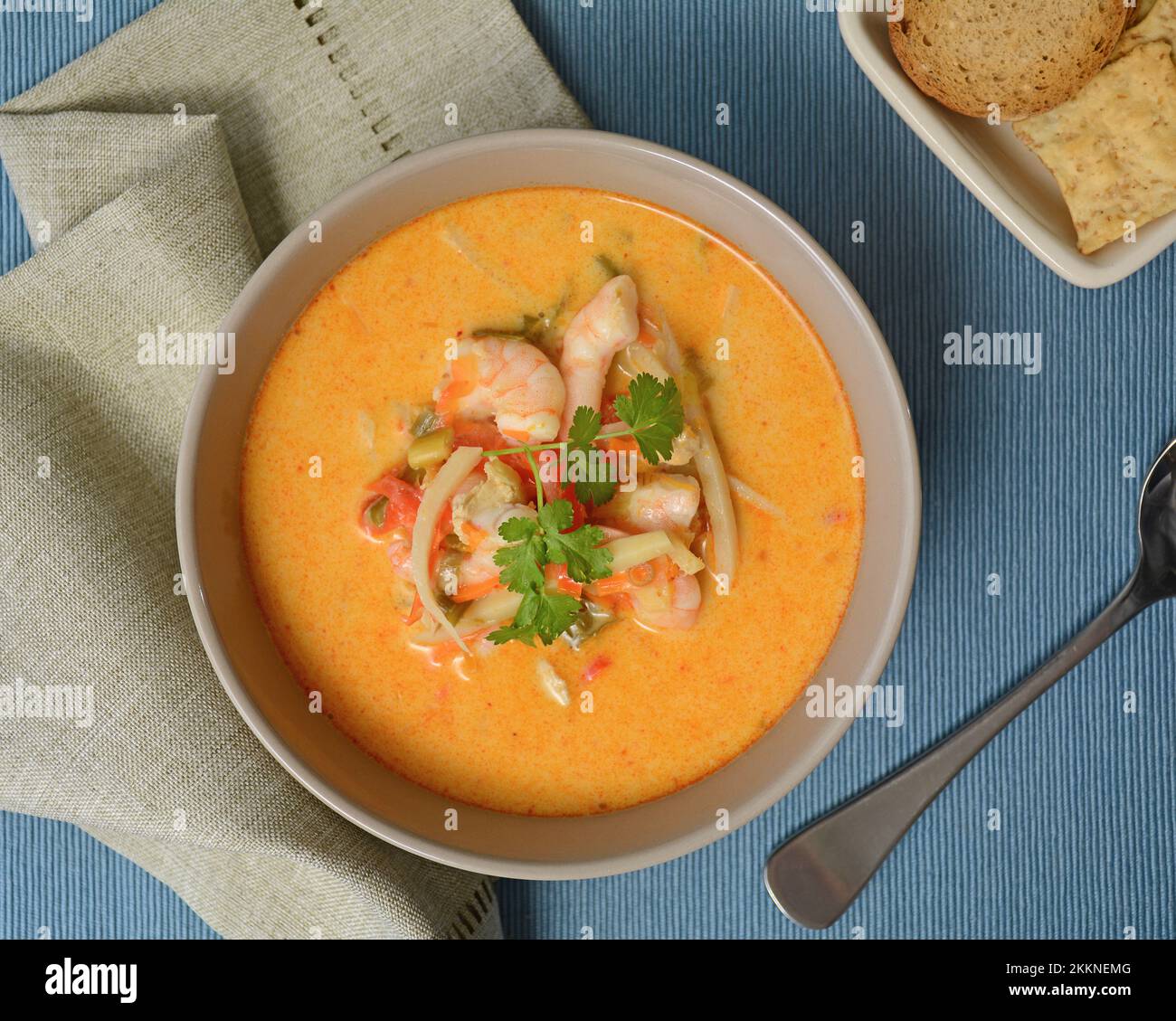 Healthy spicy Thai prawn soup with crackers on blue background in ...