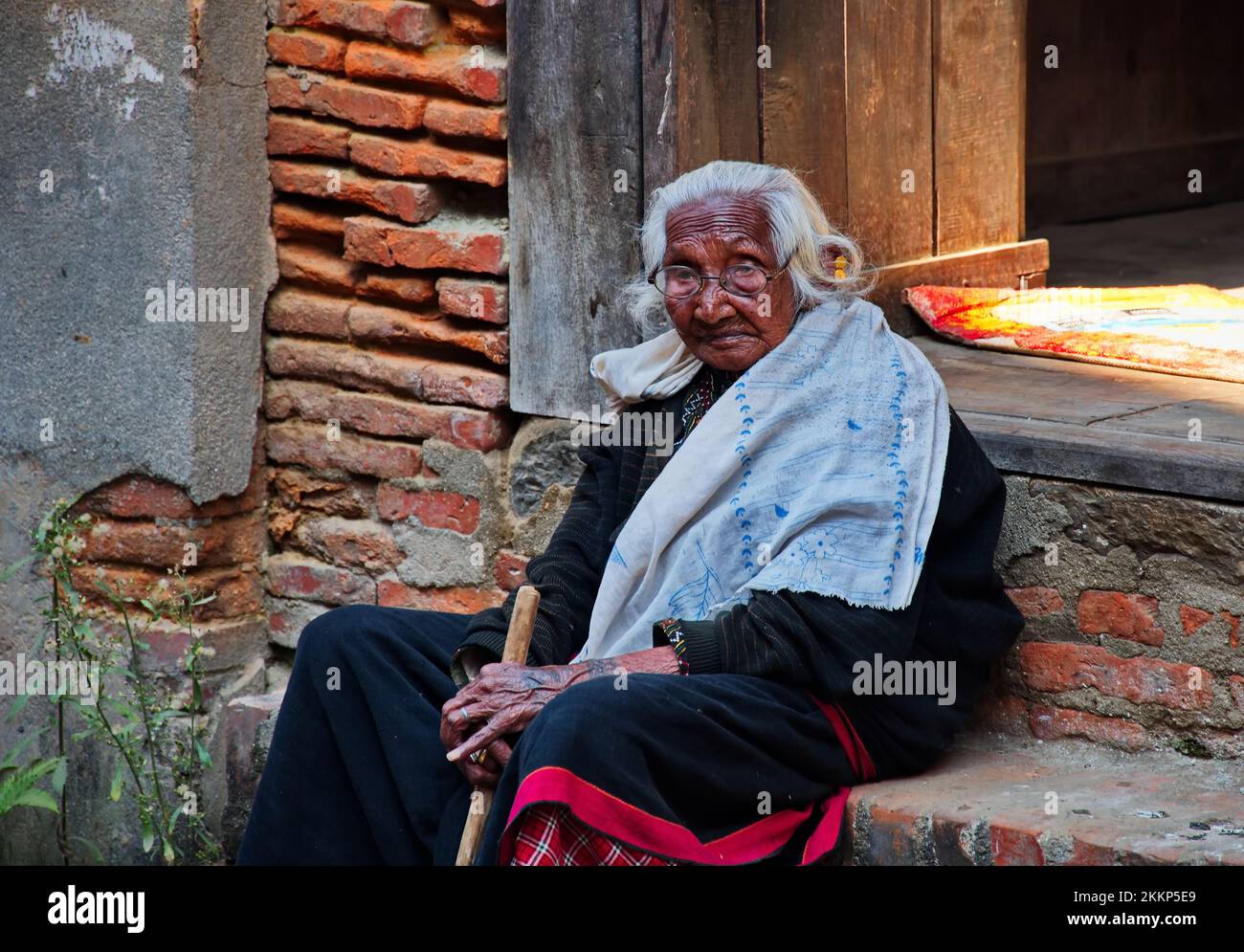 Portrait of senior Nepali woman sitting on a threshold in Kathmandu ...