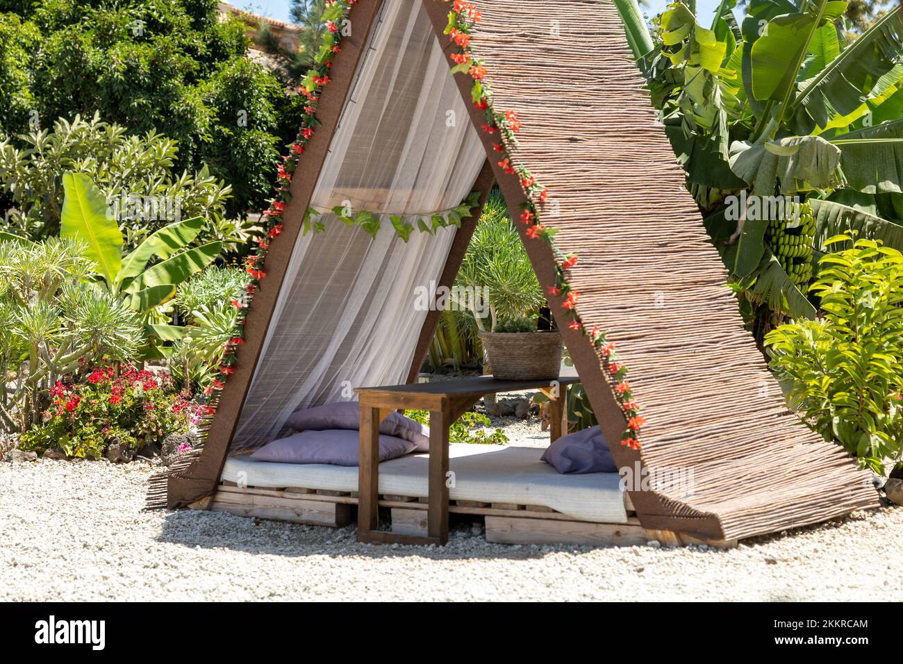 A wooden triangle-shaped gazebo with a bed and table inside isolated in ...