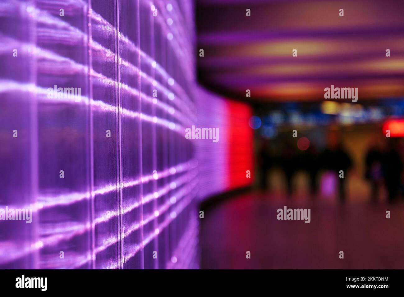 Passers-by in underground passage Passerelle, purple illuminated wall ...