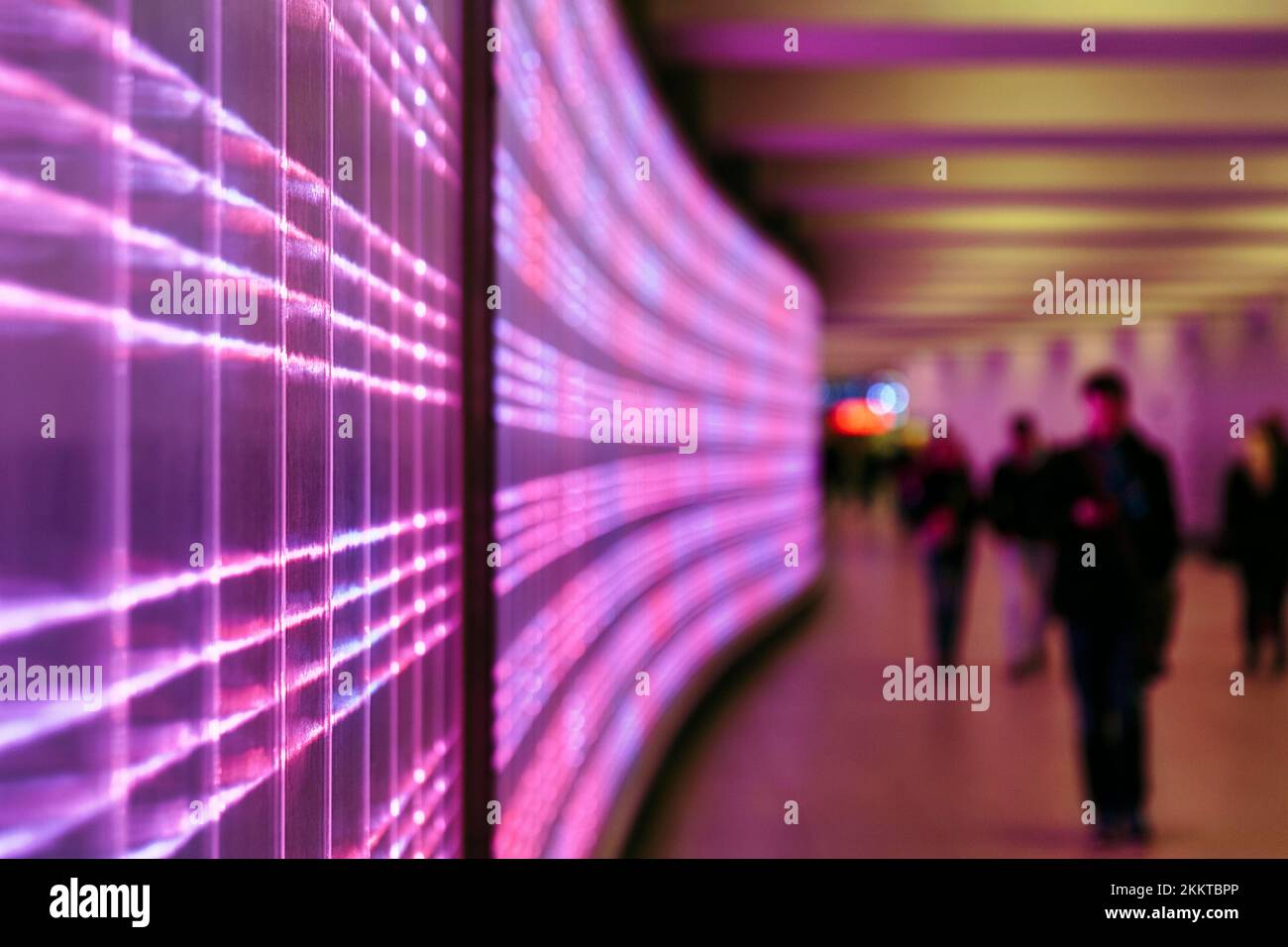Passers-by in underground passage Passerelle, pink illuminated wall ...