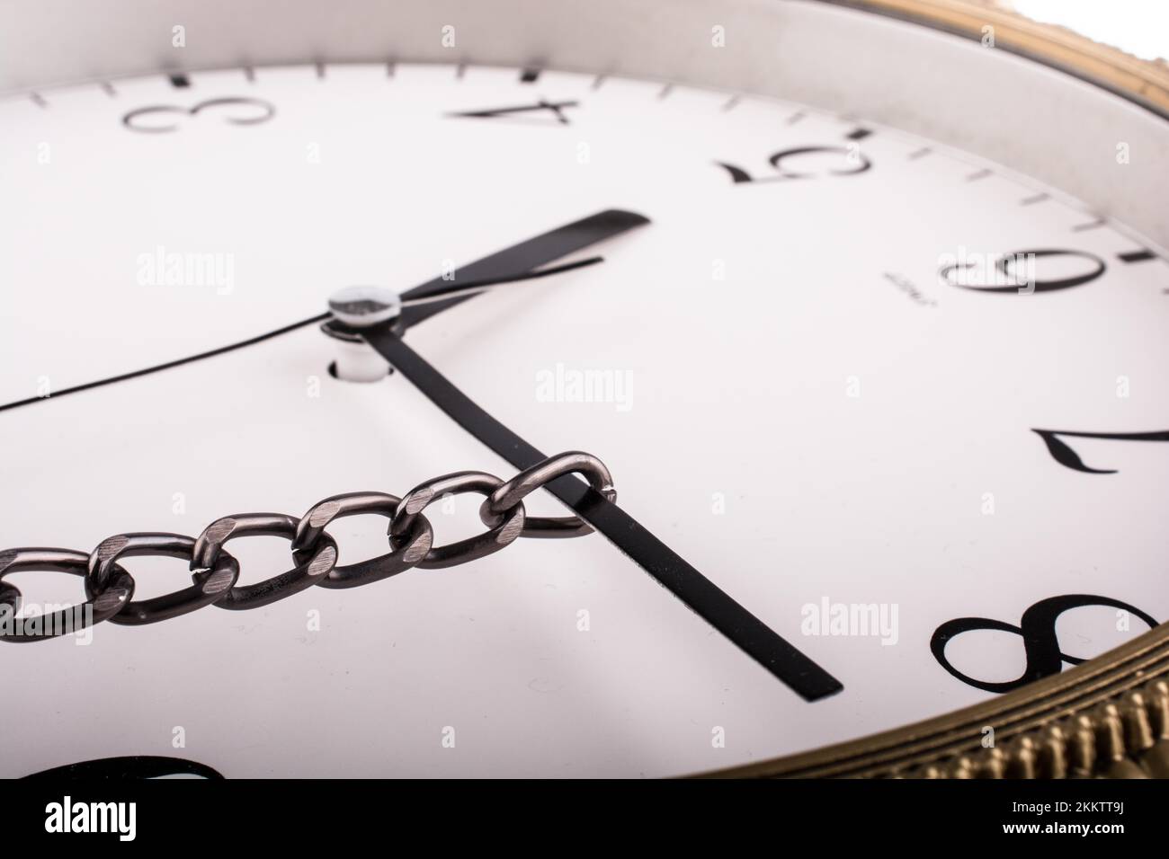 Chain tied to minute hand of a clock and pulled on a white background ...