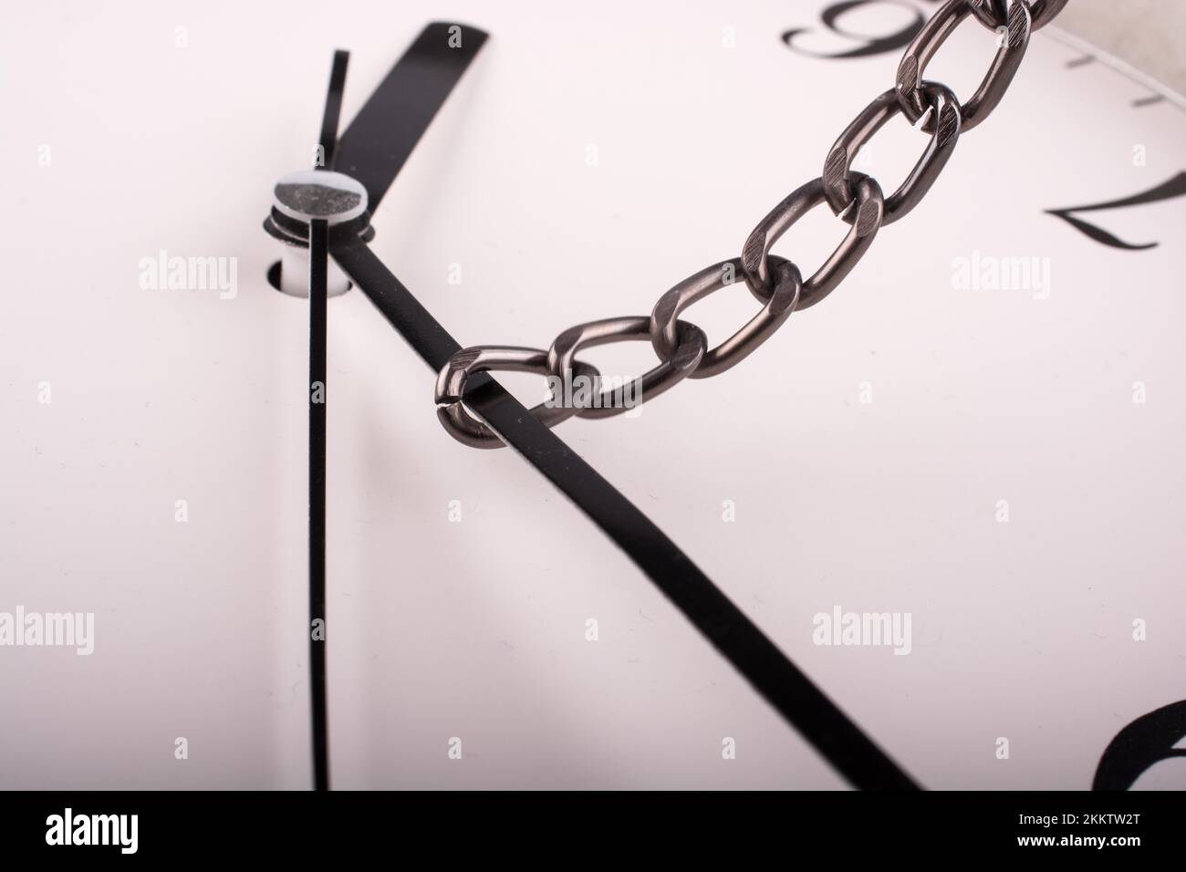 Chain tied to minute hand of a clock and pulled on a white background ...