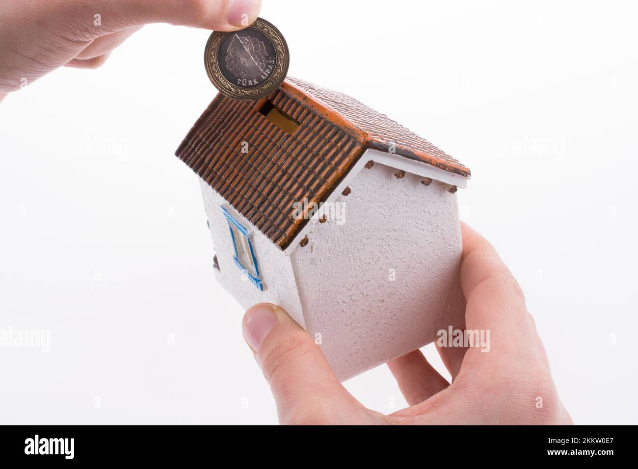 Hand dropping coin into the moneybox in the shape of a model house ...
